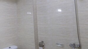 Casa de banho com sanita, chuveiro e suporte para papel higiénico.
