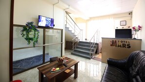 Um hall de hotel com balcão de recepção, escada, sofá, mesa de centro e televisão.