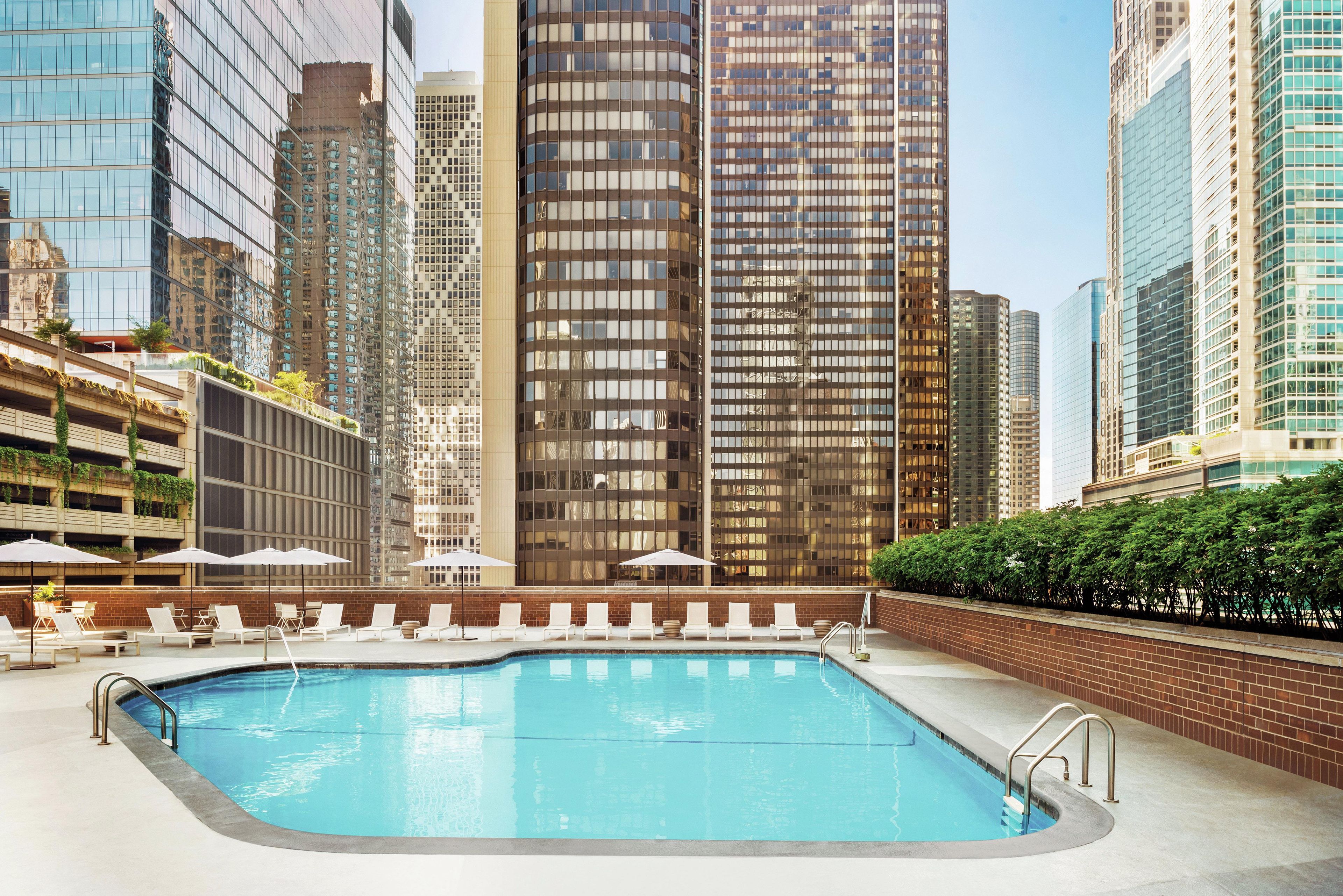 Piscina no terraço com espreguiçadeiras e guarda-sóis, rodeada por edifícios altos.