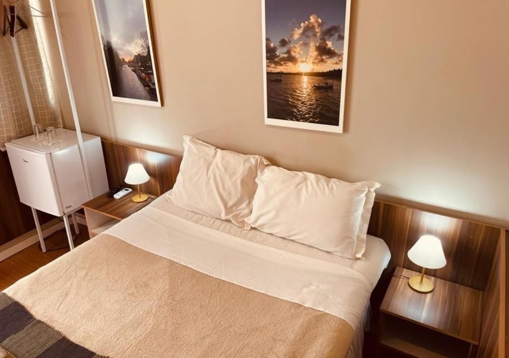Quarto de hotel com cama, mesas de cabeceira, escrivaninha e uma cadeira.