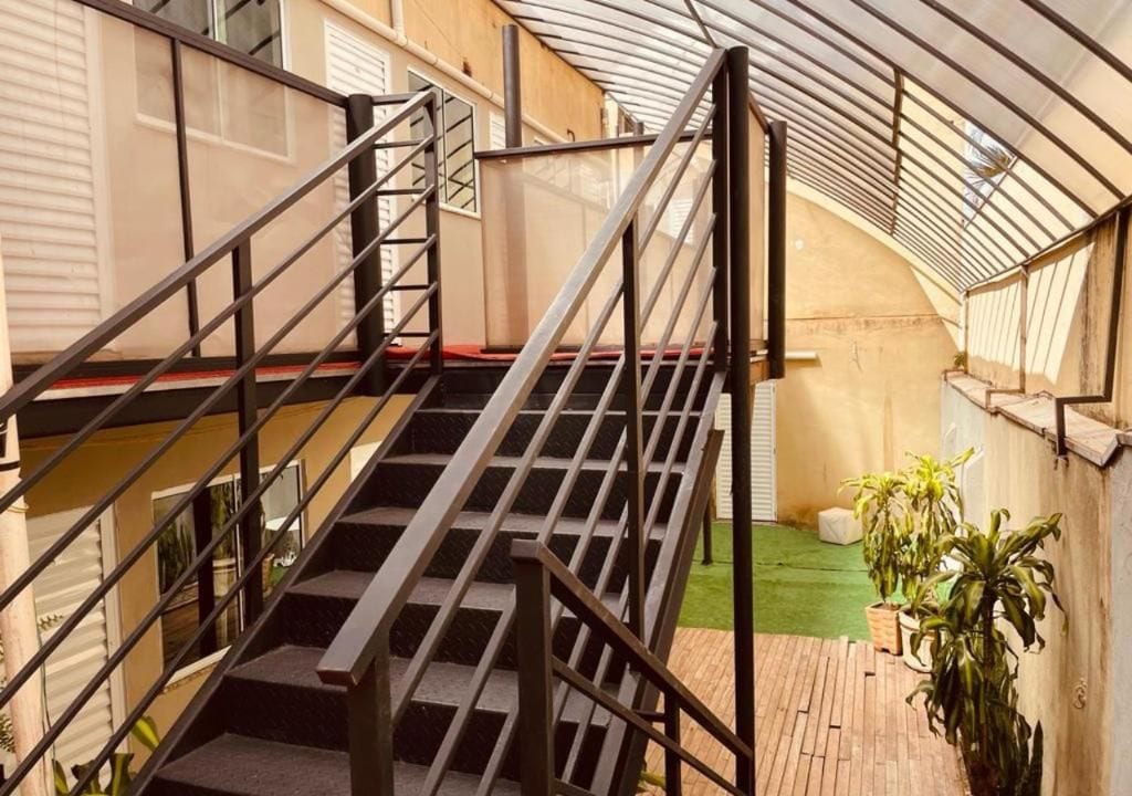 Escadaria com guarda-corpos de metal que leva a uma área externa coberta, com gramado verde e plantas em vasos.