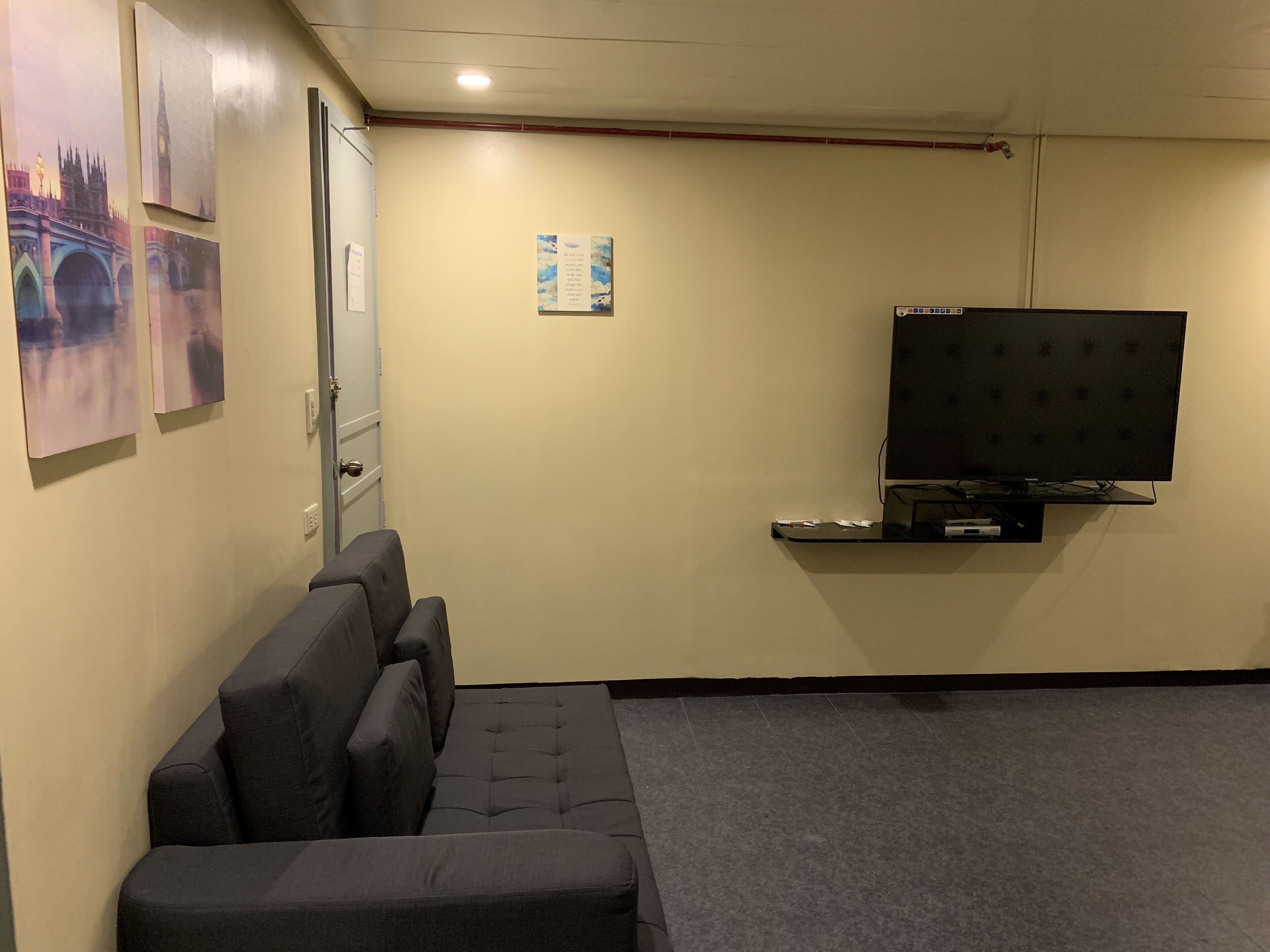 Quarto com um sofá cinzento, uma televisão de tela plana na parede e um cartaz de uma ponte.