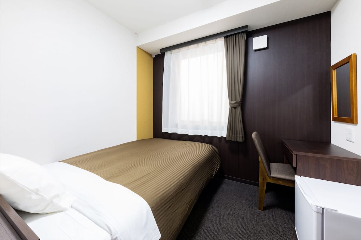 Quarto de hotel com uma cama, uma escrivaninha e uma cadeira.