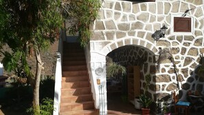 Um edifício de pedra com uma escadaria que leva a uma entrada, plantas em vasos e um candeeiro.