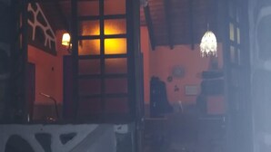 Um quarto com pouca luz, uma porta de madeira e uma janela. Um candelabro pendurado no teto.