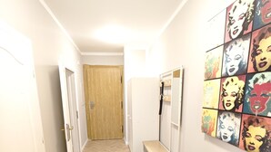 Um corredor com piso em padrão herringbone, paredes brancas e uma porta de madeira no final.