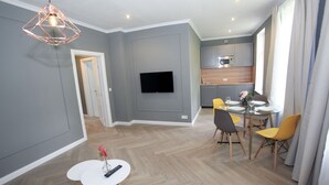 Uma sala de estar moderna com uma TV de tela plana, uma área de jantar com cadeiras amarelas e uma cozinha com armários cinzas.