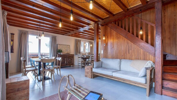 Um quarto aconchegante com teto de madeira, um sofá, uma mesa de jantar com cadeiras e uma escada.