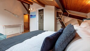 Quarto com claraboia, cama com almofadas estampadas, radiador e escada de madeira.