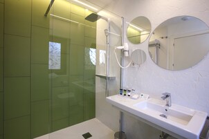 Um banheiro moderno com chuveiro em azulejos verdes, pia branca e duas espelhas.