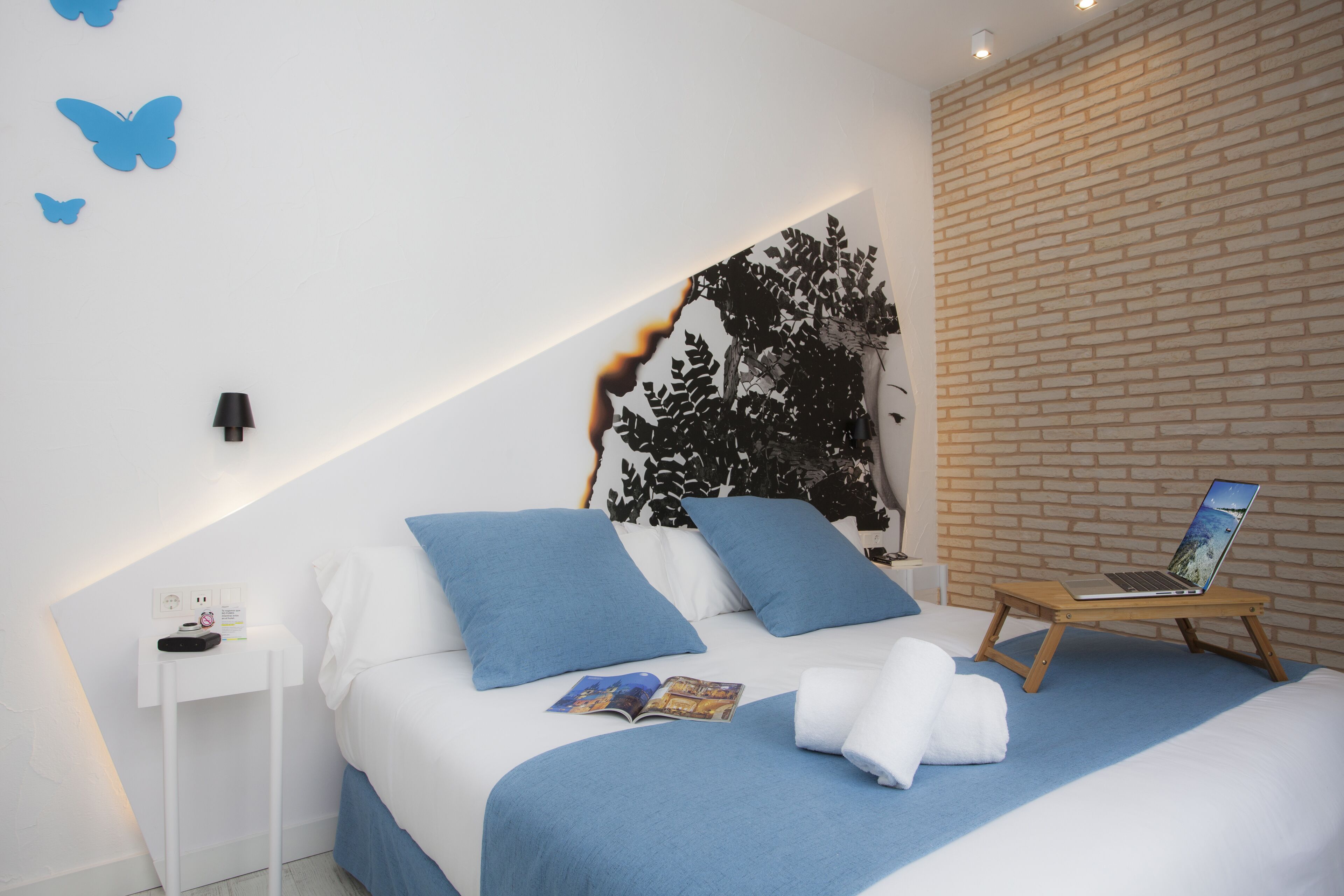 Quarto moderno com cama, um laptop sobre um suporte de madeira e parede com padrão de tijolos.