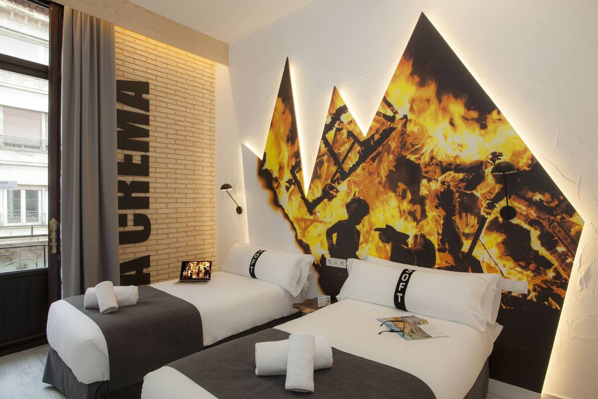 Quarto de hotel com duas camas, uma parede de tijolos e uma grande obra de arte com tema de fogo na parede.