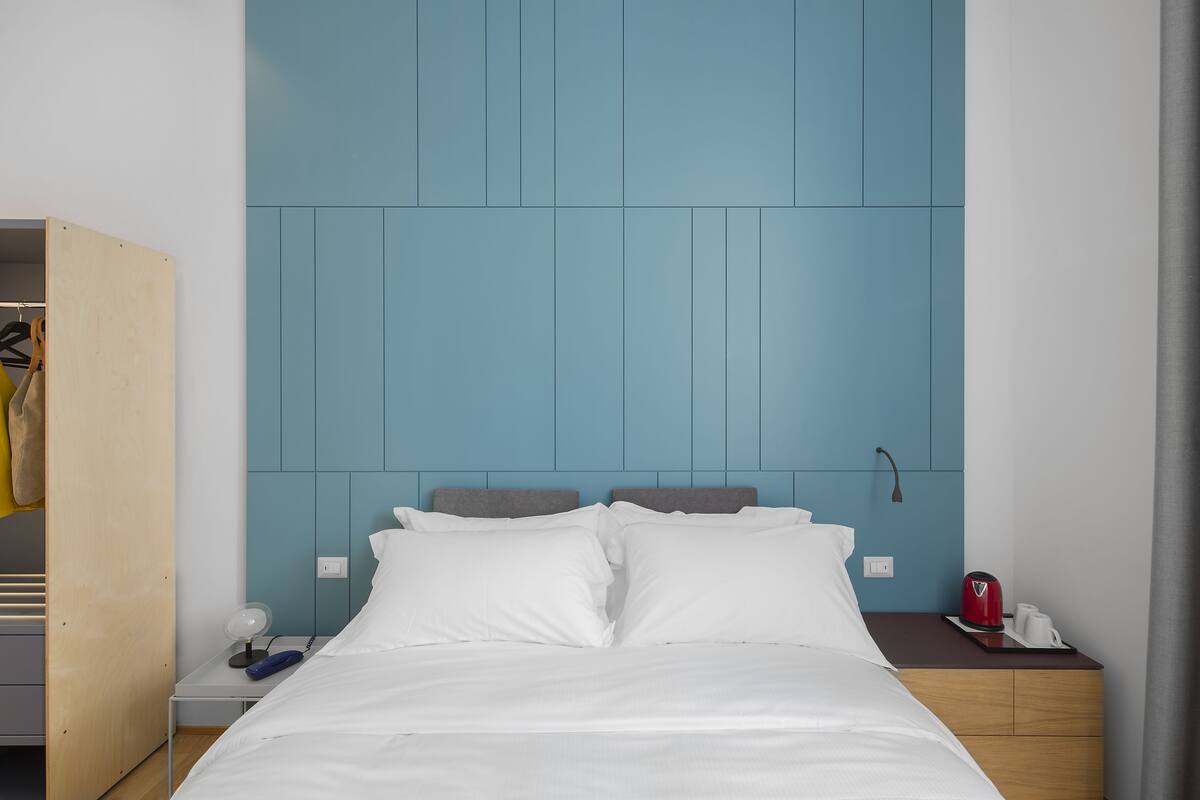 Quarto de hotel com cama, mesa de cabeceira, guarda-roupa e parede azul.