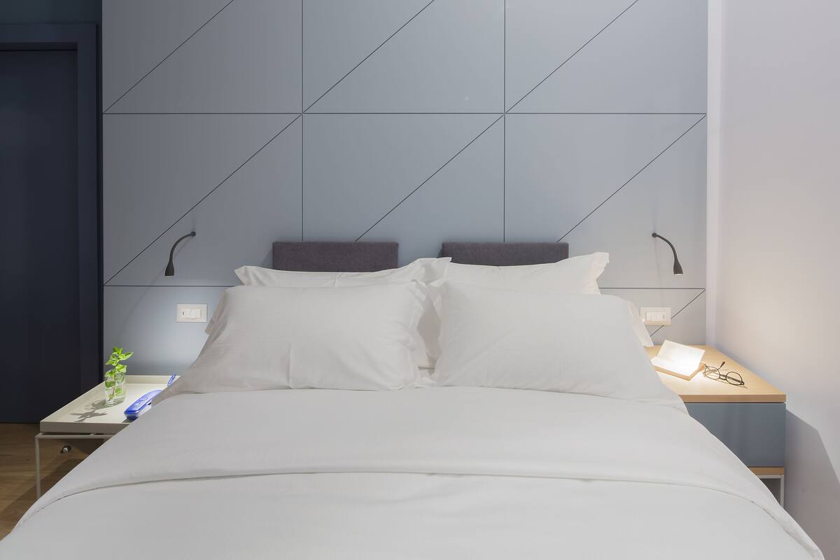 Quarto moderno com cama, mesas de cabeceira e parede com padrão geométrico.