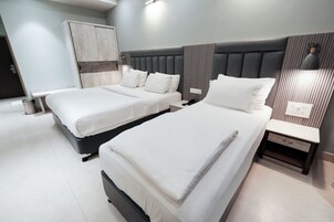 Quarto de hotel com duas camas, um guarda-roupa, mesas de cabeceira e uma luminária.