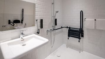 Uma casa de banho moderna com azulejos brancos tipo metrô, uma pia branca, um espelho, um porta-toalhas preto e um chuveiro com chuveiro manual.