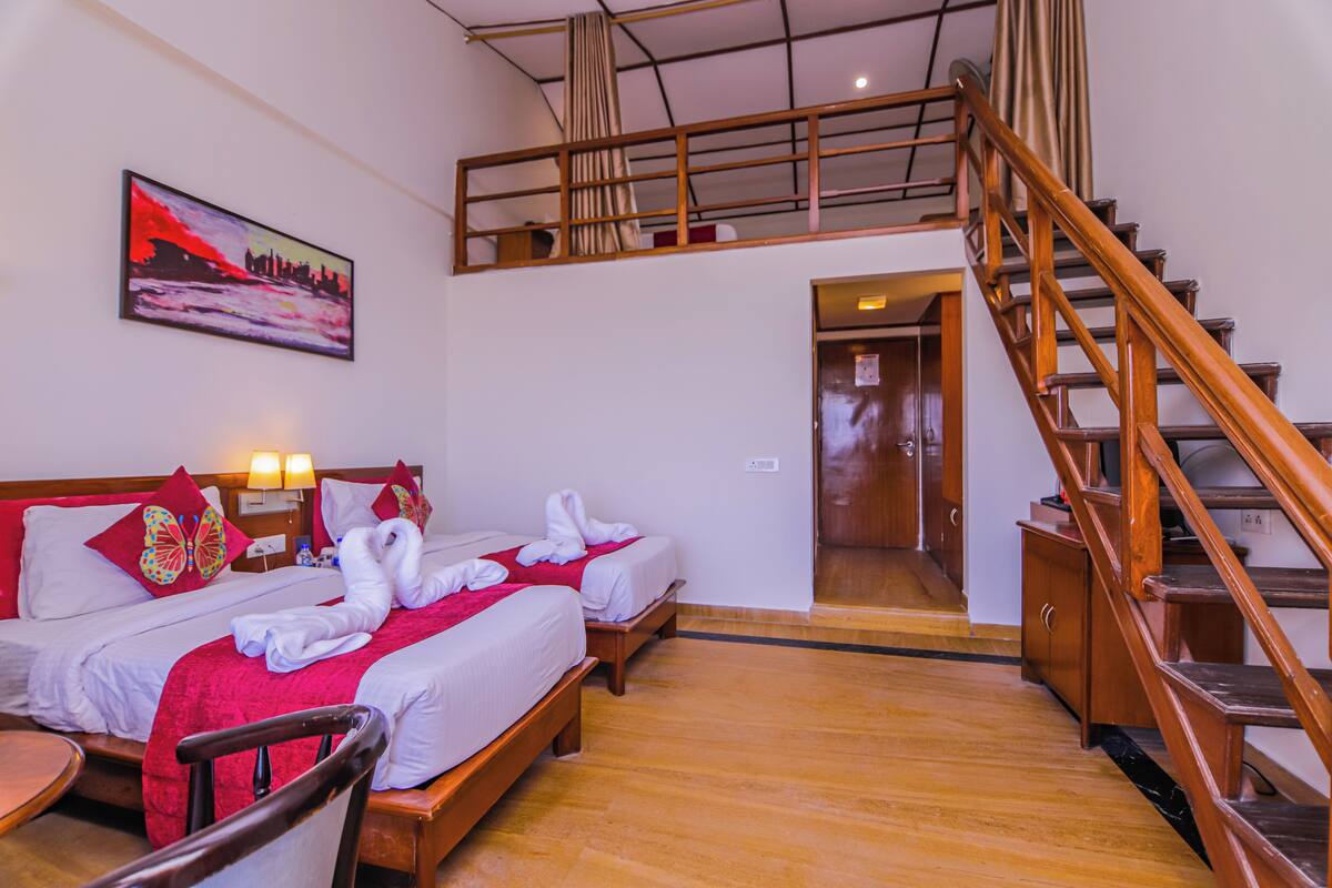Quarto de hotel com duas camas, escada de madeira e uma pintura da paisagem urbana na parede.