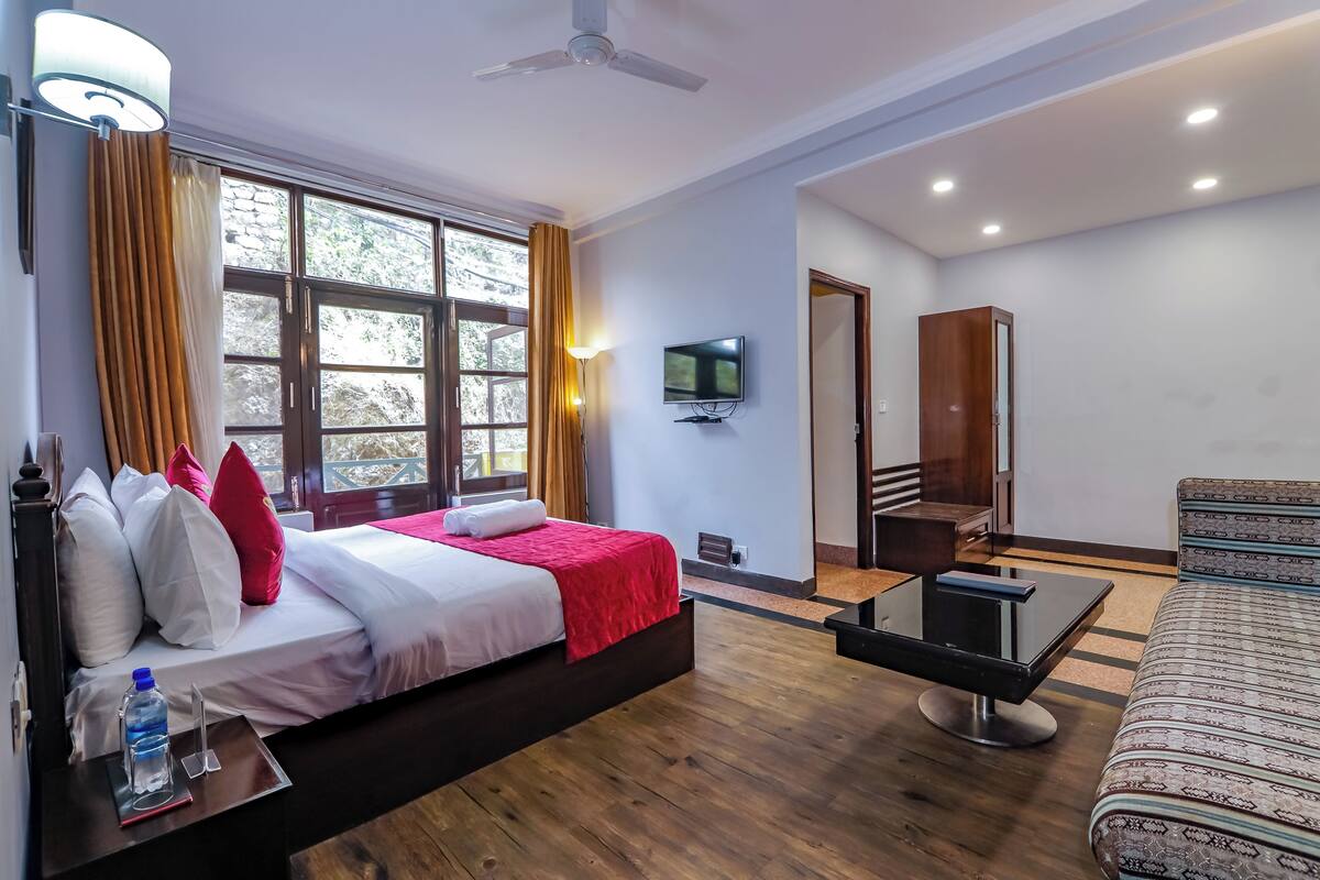 Quarto de hotel moderno com cama, sofá, televisão e mesa de jantar.