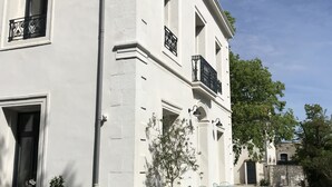 Um edifício de dois andares com varanda, plantas em vasos e área de estar ao ar livre.