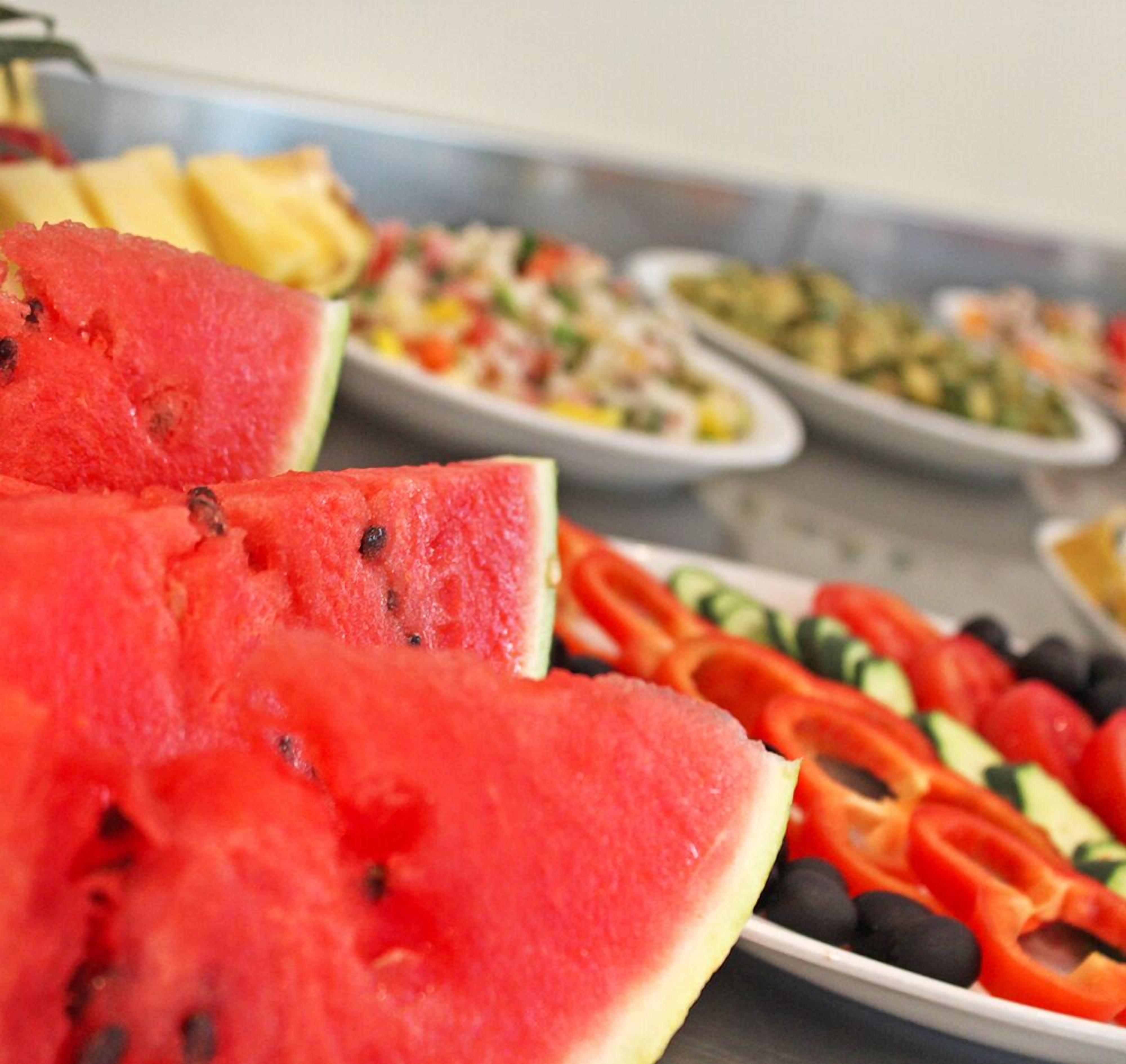 Buffet com diversos alimentos, incluindo melancia, vegetais e saladas.