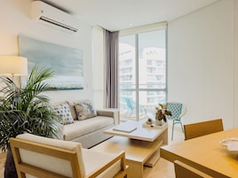 Uma sala de estar moderna com sofá, mesa de centro e poltronas, uma janela grande com cortinas e uma planta em vaso.