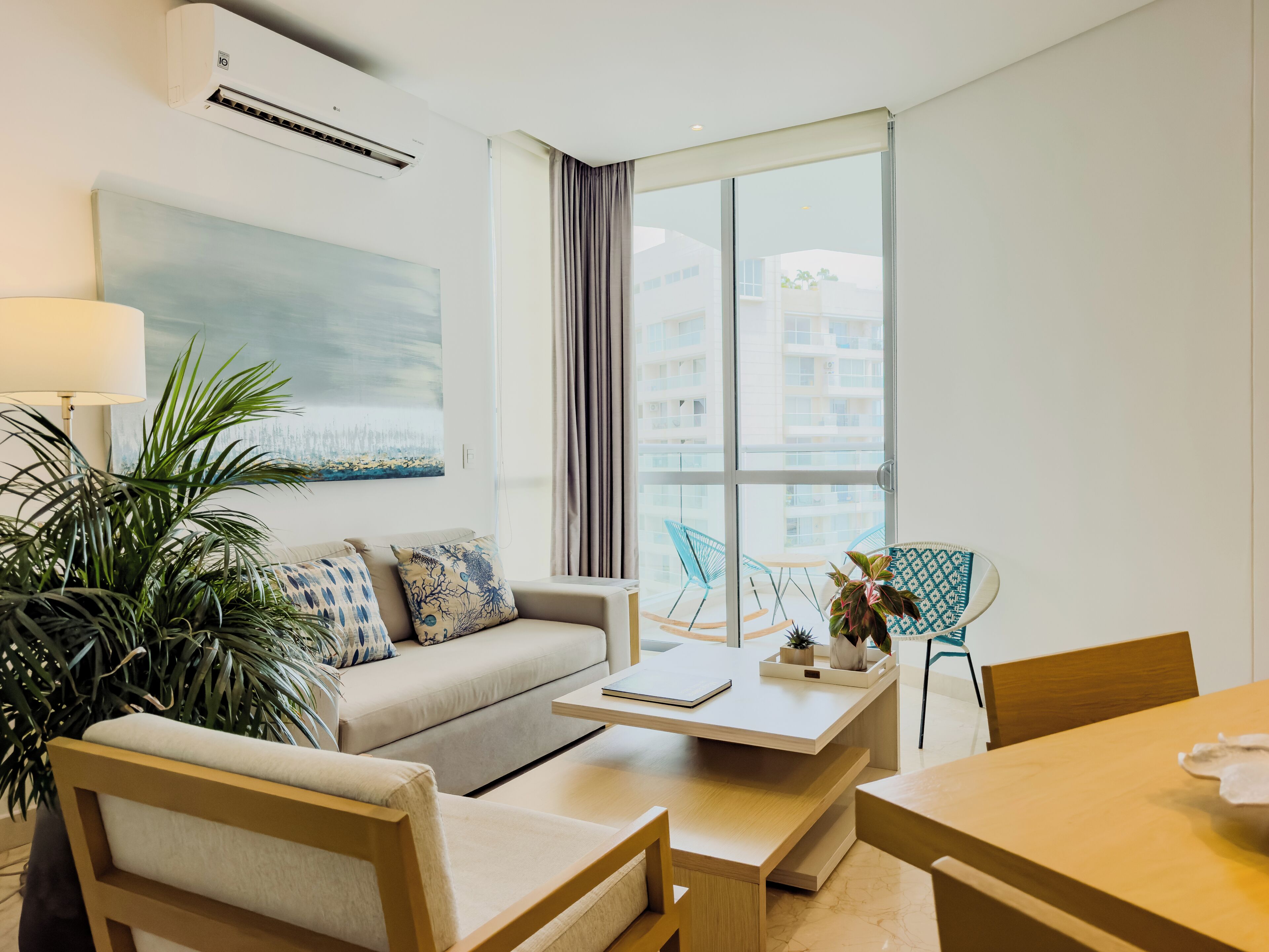 Uma sala de estar moderna com sofá, mesa de centro e cadeiras, uma janela grande com cortinas e um vaso de planta.
