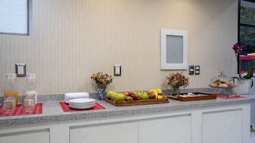 Uma bancada de cozinha com um suporte de frutas, pratos e um vaso com flores.