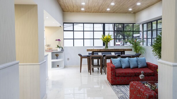 Uma sala de estar espaçosa, com um sofá vermelho, uma mesa de jantar com cadeiras e uma janela grande que traz luz natural.