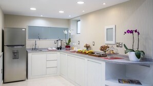 Uma cozinha moderna com armários brancos, uma geladeira de aço inoxidável e um balcão com frutas e flores.