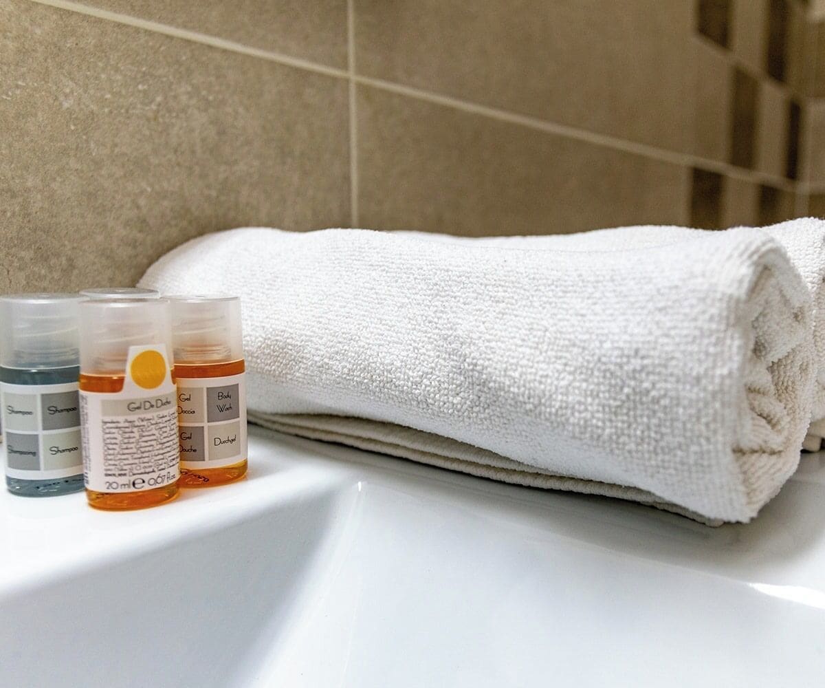 Casa de banho com toalha branca, dois frascos de champô e um frasco de gel de banho.