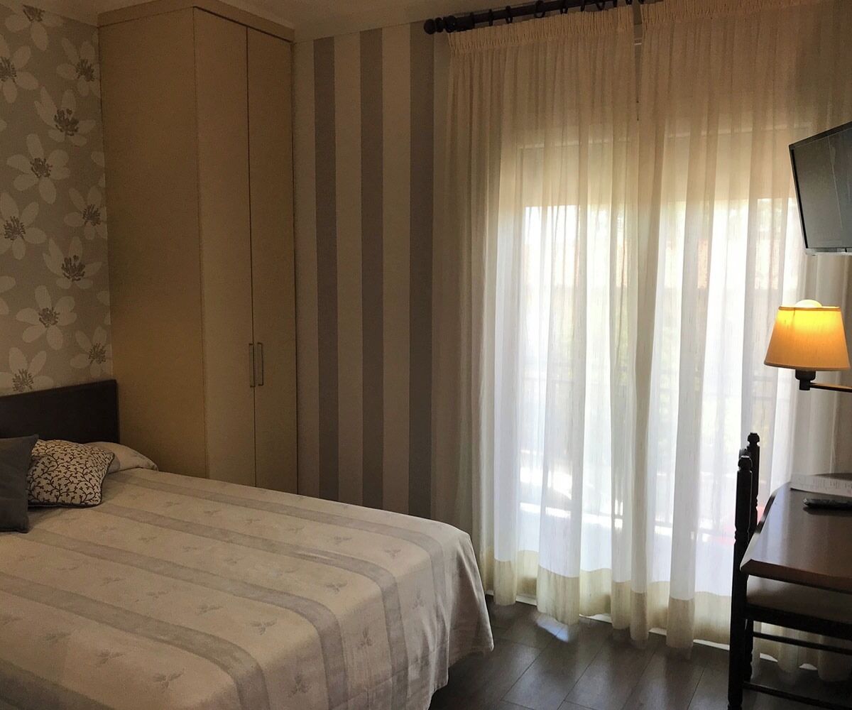Quarto com cama, guarda-roupa, escrivaninha e cortinas.