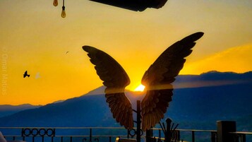 Pôr do sol com silhueta de asas e montanhas ao fundo.