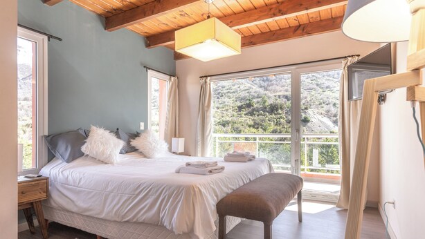 Quarto com cama, um banco, mesa de cabeceira e vista para o exterior.