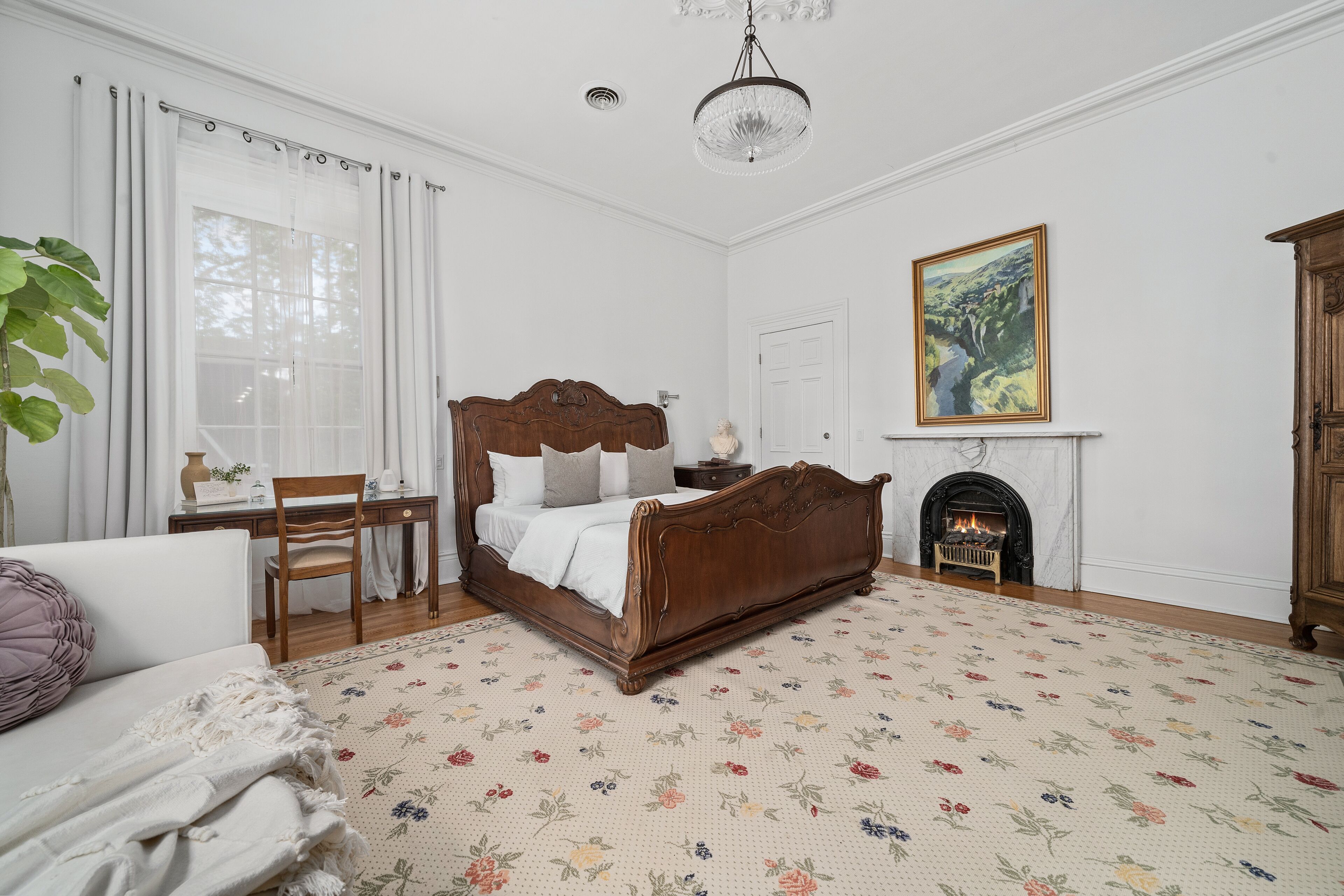 Quarto com uma cama grande, uma escrivaninha, uma cadeira, lareira e um quadro na parede.