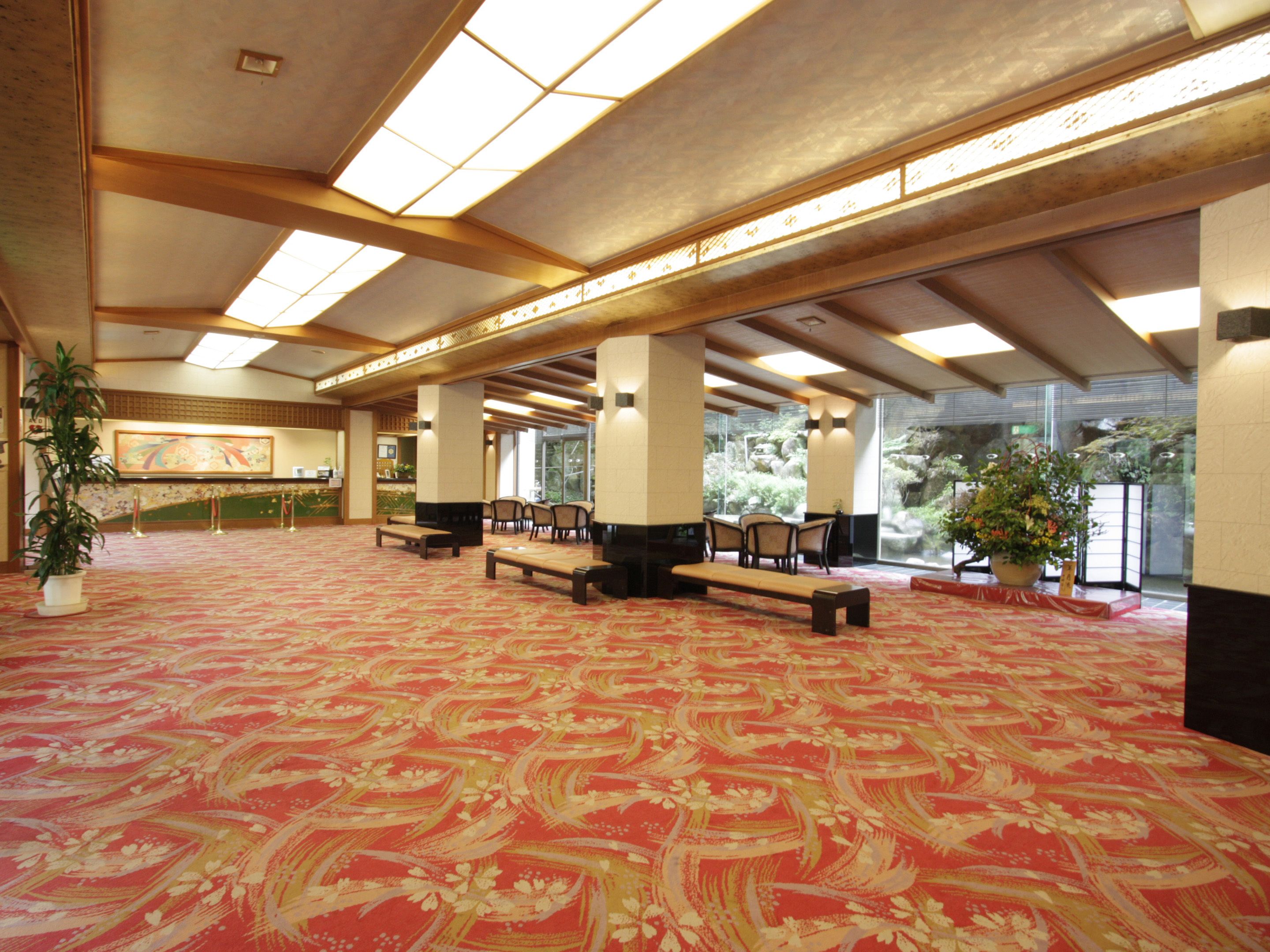 Um hall amplo com carpete estampado, bancos de madeira e plantas em vasos.