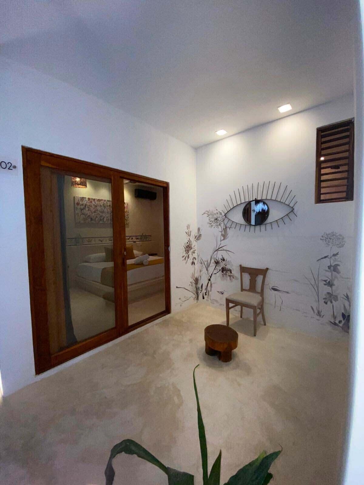 Quarto com porta de vidro deslizante que dá para um quarto, uma cadeira de madeira, uma pequena mesa redonda e um objeto decorativo pendurado na parede.