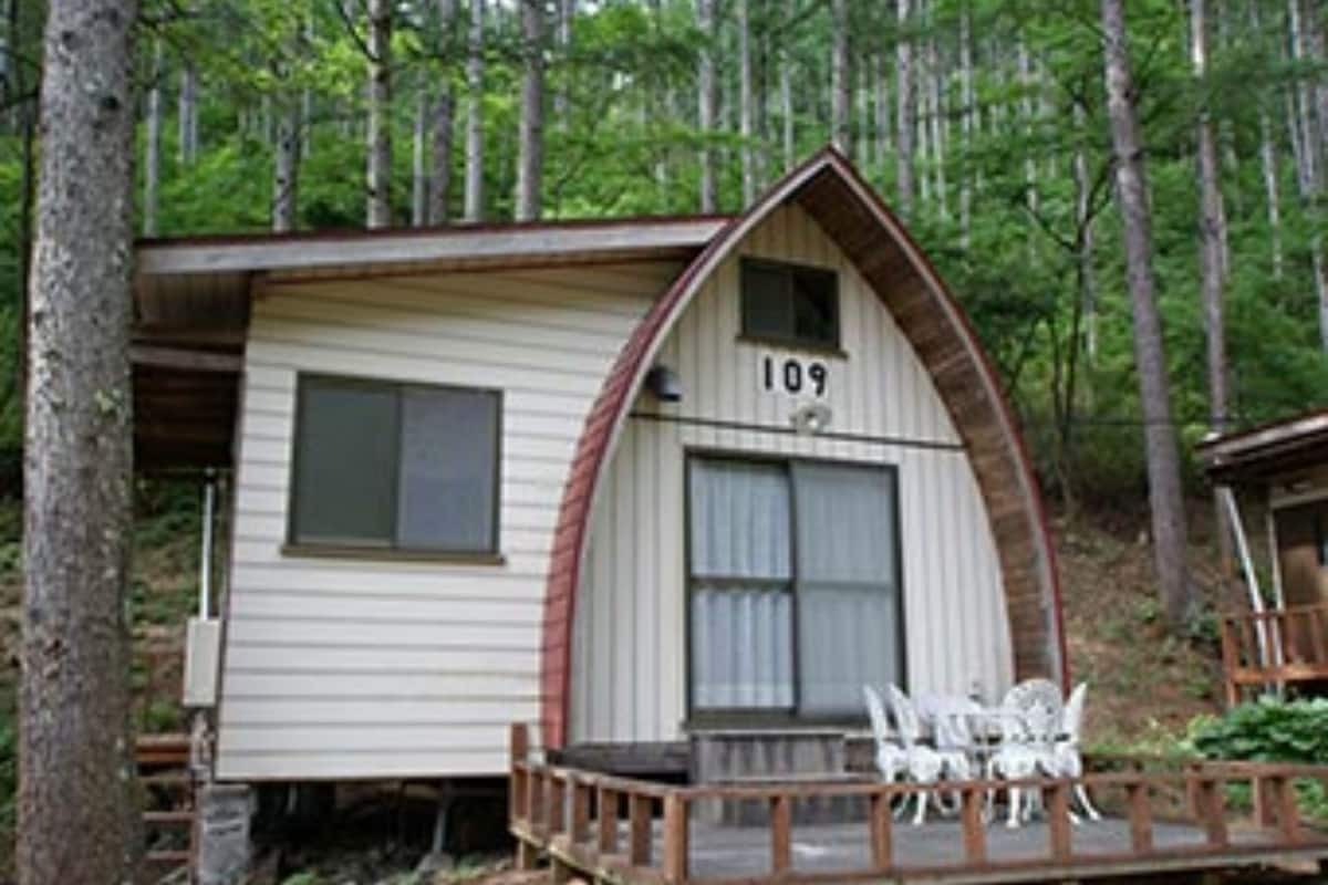 Uma cabana com o número 109 na fachada, um alpendre com cadeiras e um cenário de mata ao fundo.