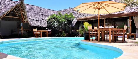 Uma área de piscina com estrutura de palha, cadeiras de descanso e guarda-sóis.
