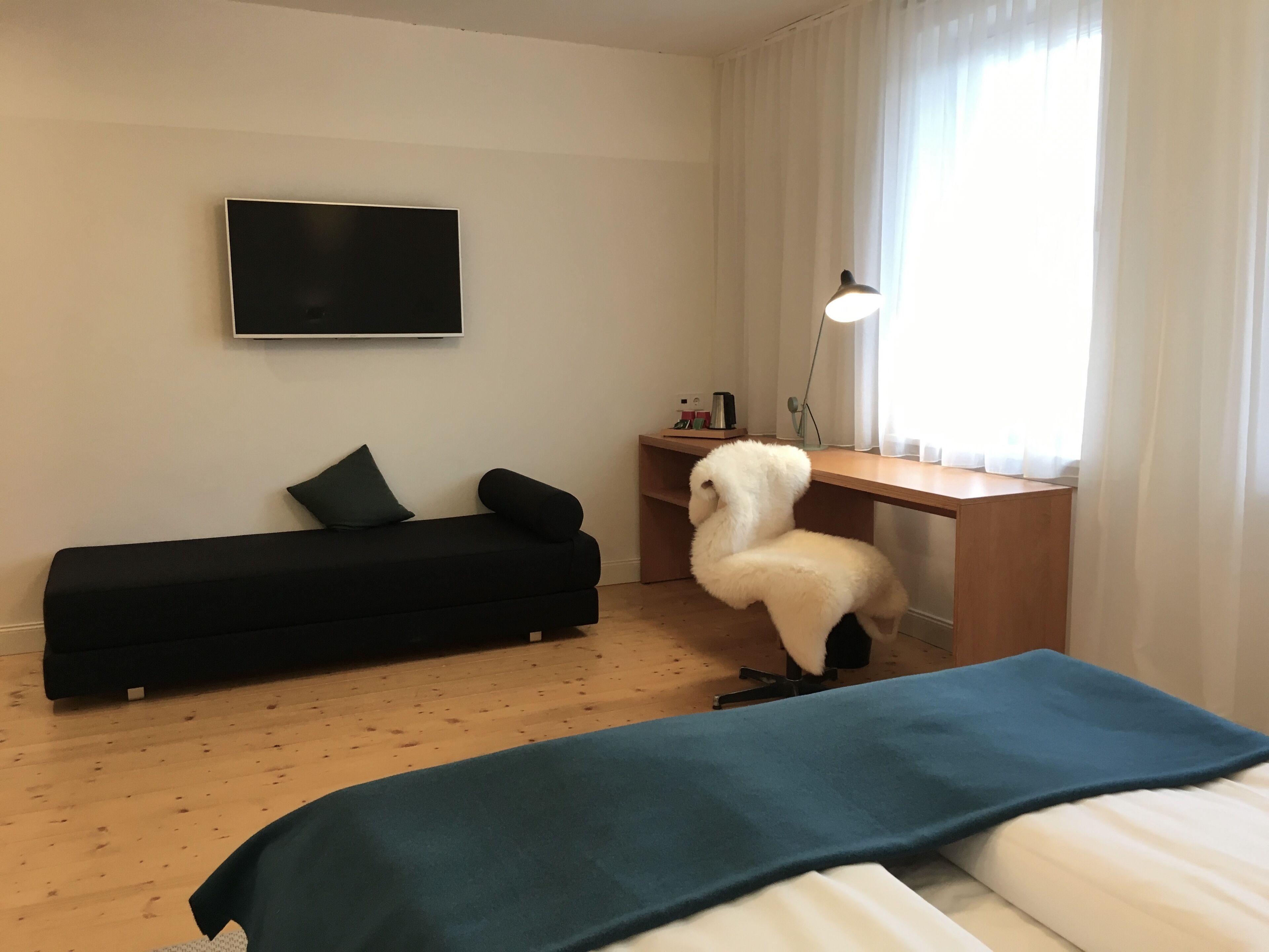 Quarto de hotel moderno com uma cama, escrivaninha, cadeira, sofá, televisão e janela com cortinas.