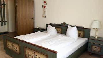 Cama bem arrumada em quarto com piso de madeira, porta de madeira, mesa de cabeceira pequena com abajur e telefone fixado na parede.