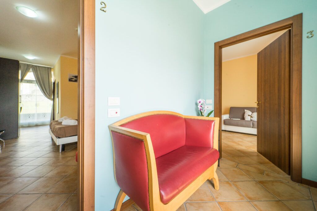 Um quarto com um sofá de couro vermelho, uma porta de madeira e piso ladrilhado.