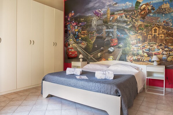 Quarto com cama, mesas de cabeceira, guarda-roupa e um mural com vista para a cidade.