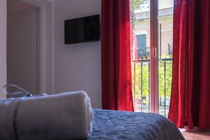 Quarto de hotel com cama, TV fixada na parede e varanda com cortinas vermelhas.