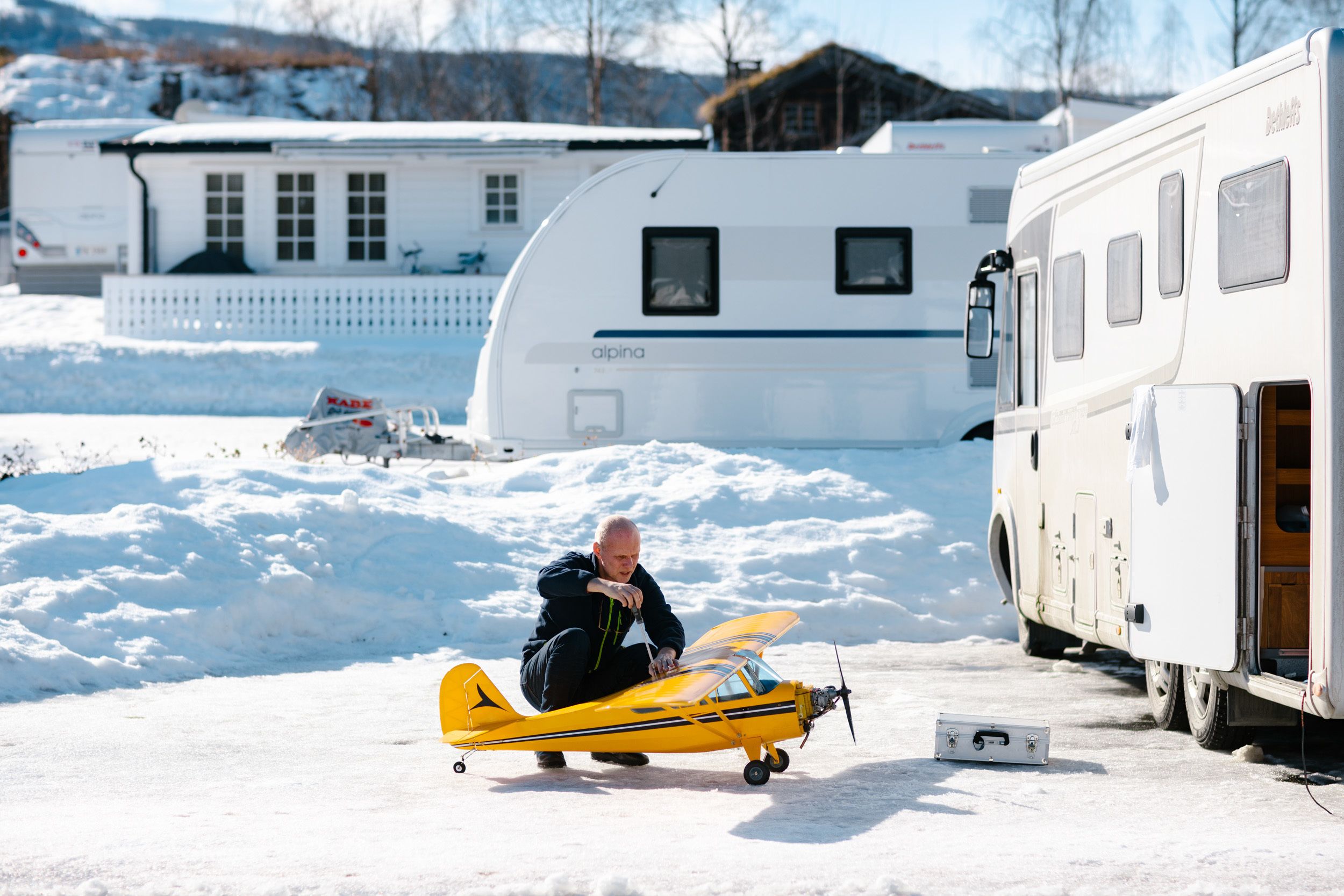 Solo coberto de neve com um pequeno avião amarelo e uma RV branca.