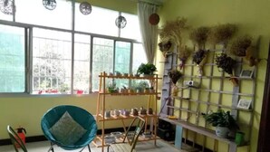 Um quarto com uma janela grande, uma cadeira, uma estante com plantas e uma pequena mesa.