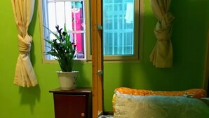 Quarto com colcha estampada, planta na mesa de cabeceira e janela com cortinas.