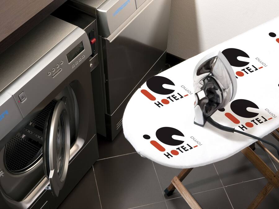 Uma área de lavanderia moderna com máquina de lavar e tábua de passar, exibindo o logotipo do Hotel.