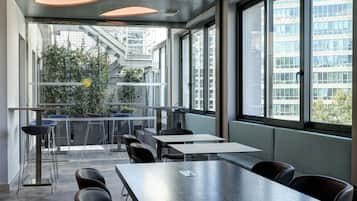 Uma sala de conferências moderna com amplas janelas, uma varanda com vegetação e vista para o horizonte urbano.