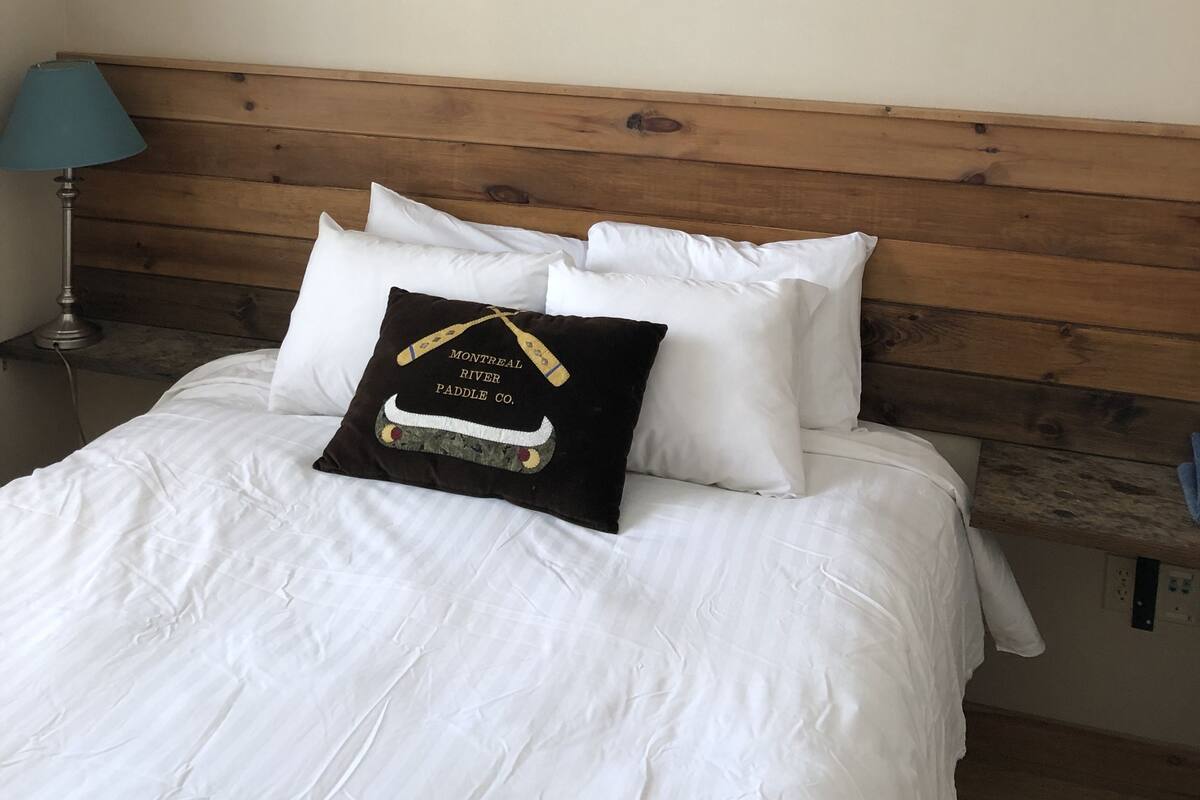 Cama bem arrumada com lençóis brancos e travesseiro preto com texto.