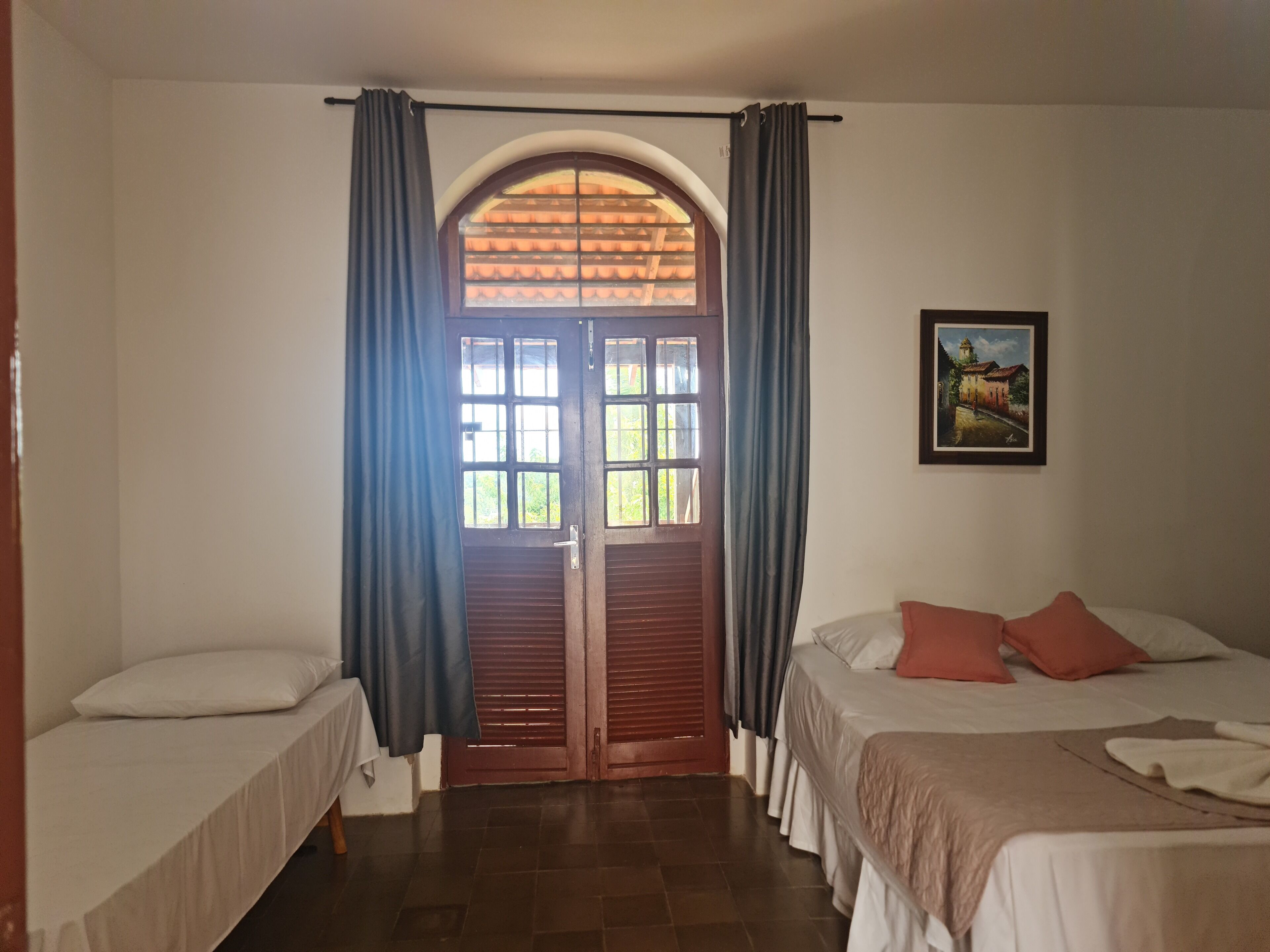 Quarto com duas camas, porta de madeira com janela e um quadro na parede.